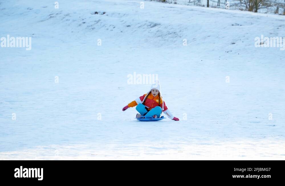 Girl rides a sledding down on snow disk a winter hill. Girl laughing ...