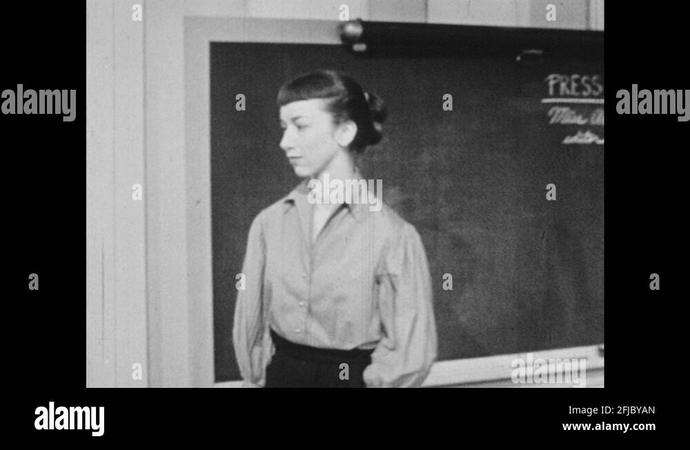 1950s: Teacher walks around desk in front of classroom. Students take ...