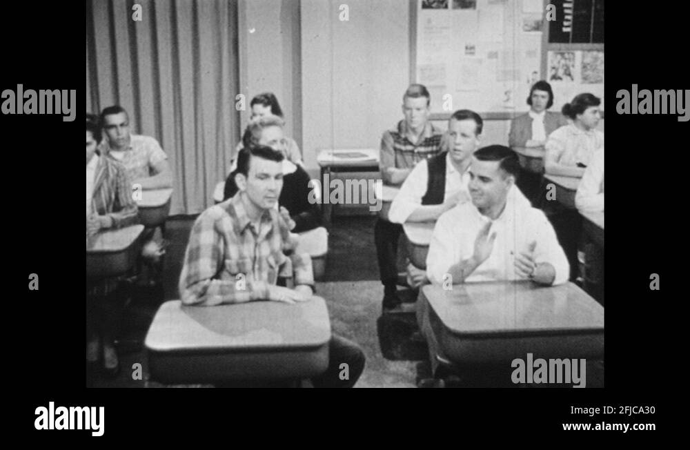 1950s: Students clap at desks in classroom. Boy in sports coat looks ...