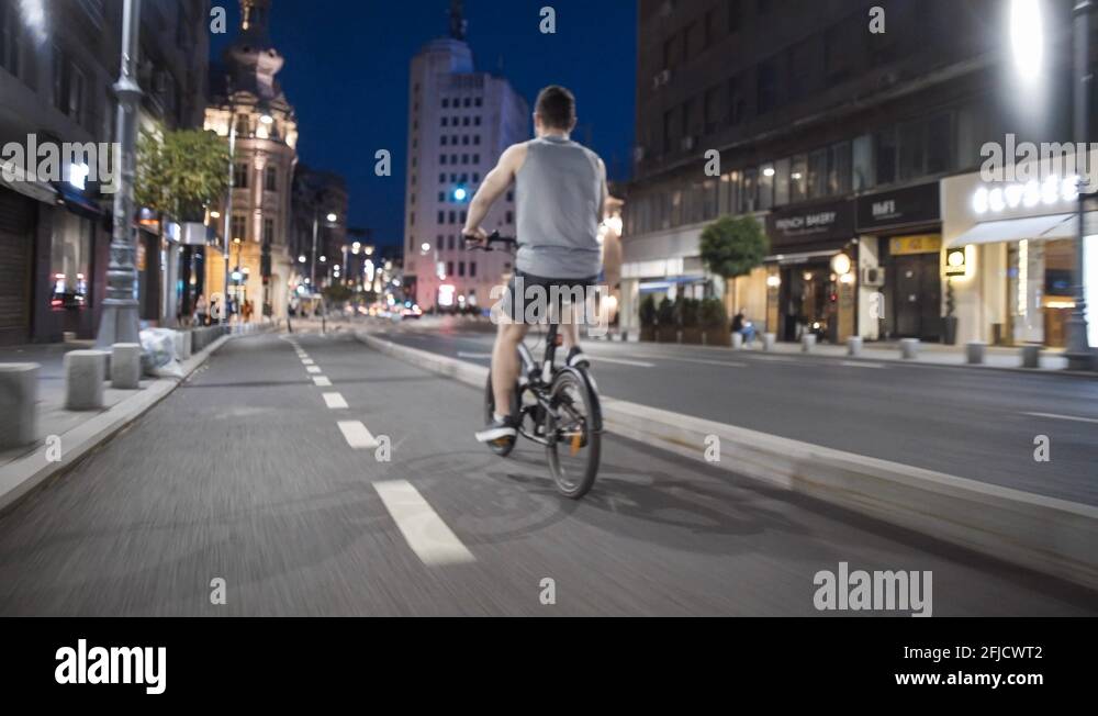 Tracking shot young man biking riding a bike on a city street at night ...