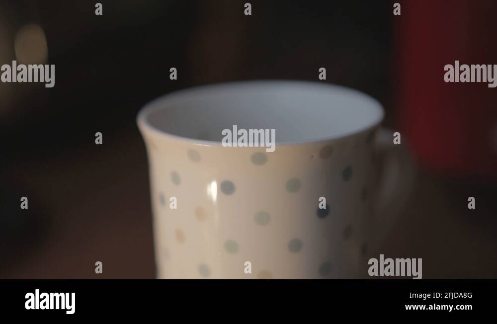 Pouring water into a white spotted mug from a red kettle with a static ...