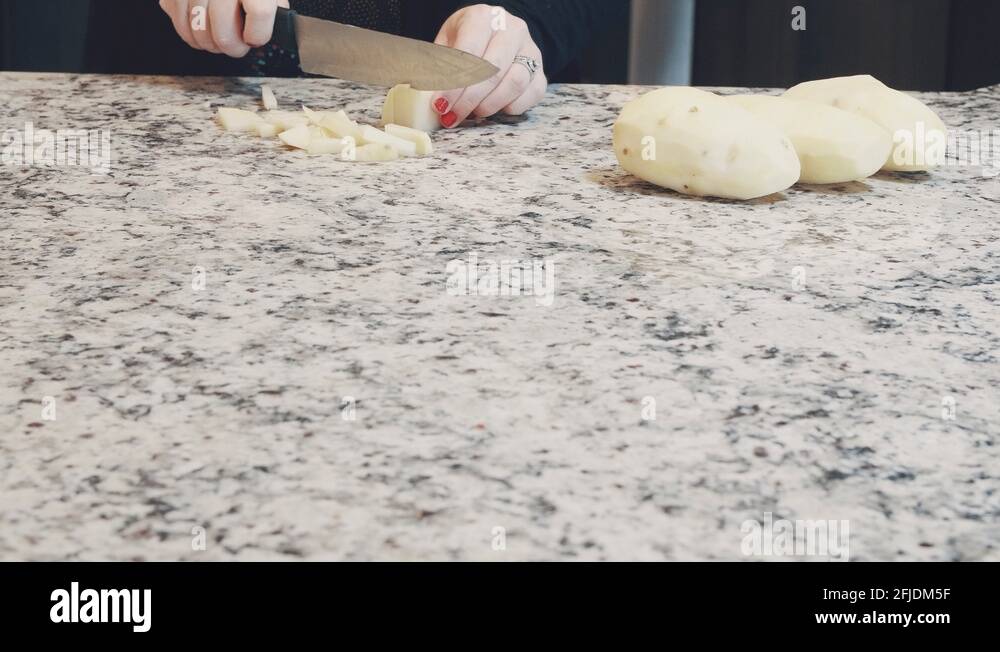 A woman chops peeled potatoes on a granite counter top in a modern ...