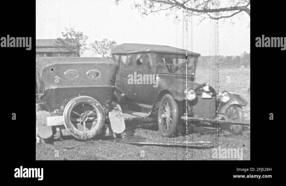 1920s: Cars struggle down rutted dirt road. Men push stuck car on dirt ...