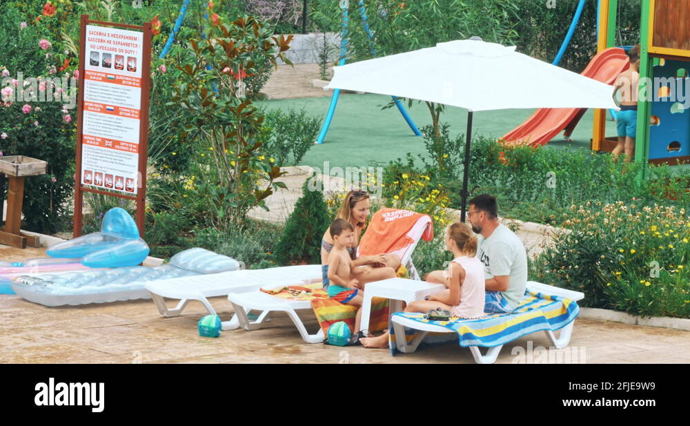 People sitting by the poolside of a resort swimming pool during summer ...