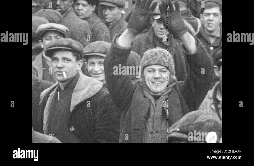 1920s: Young men crowd together at shipyard. Red Cross nurse hands out ...