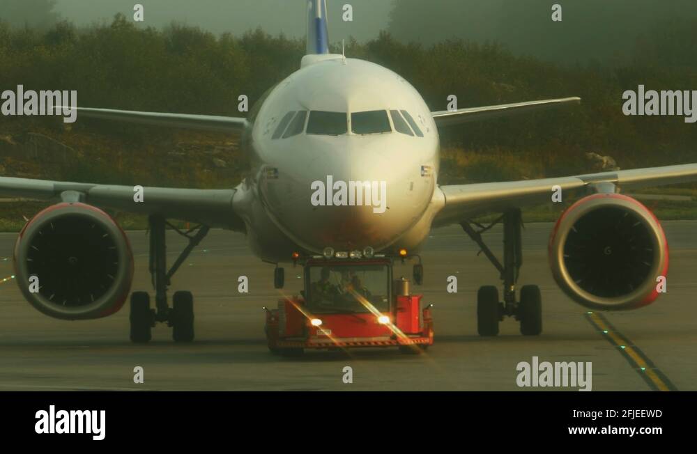 Passenger aircraft being pulled by a pushback tug vehicle on the runway ...