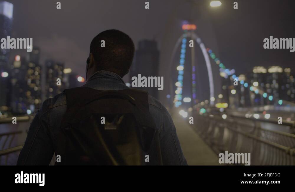Black skin African boy walks over a big bridge in the night, enjoying ...