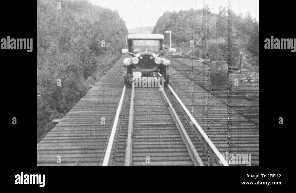1920s: Cars drive on narrow railroad trestle. Model T drives up large ...