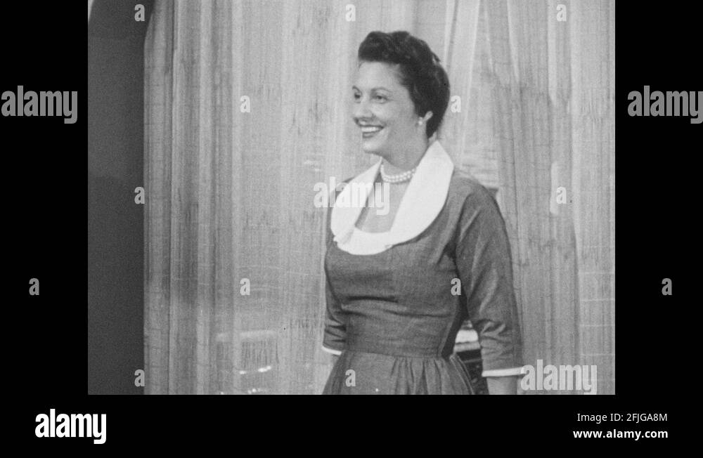 1950s: UNITED STATES: lady in house. Lady smiles at guest. Chief of ...