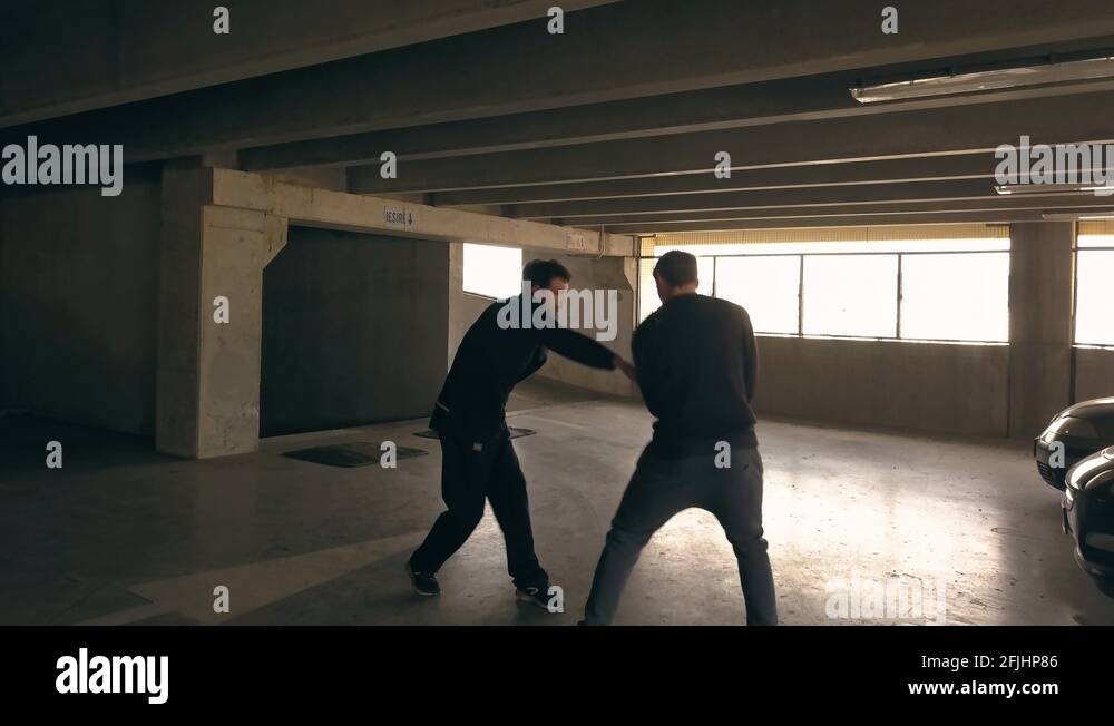 Two men dressed in black rehearse a fight scene in a parking garage ...