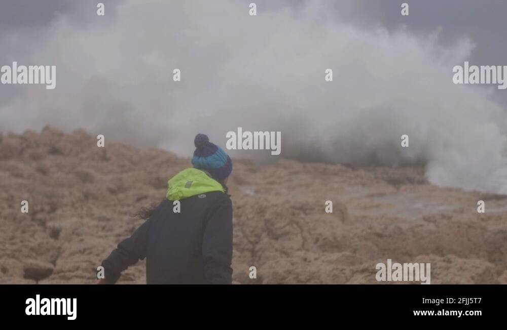 a girl in front of a storm big waves explode on the rocks in slowmotion ...