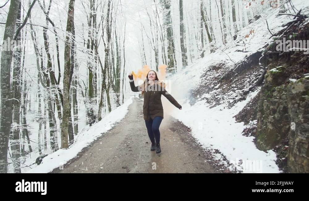 Girl running with orange smoke bomb down winter path as snow falls, 4x ...