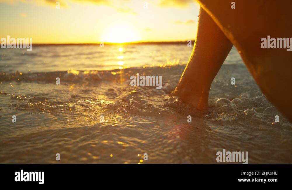 LOW ANGLE: Glassy drops of water splash around the girl's feet on sunny ...