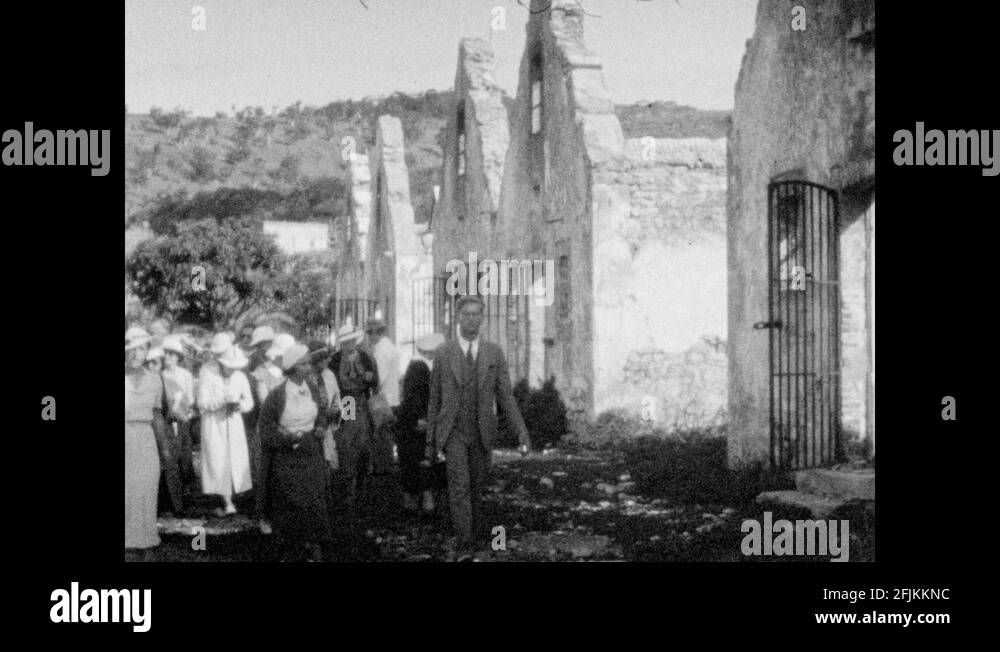 1940s: Tourists walk around old prison, bars on windows. Man holds ...