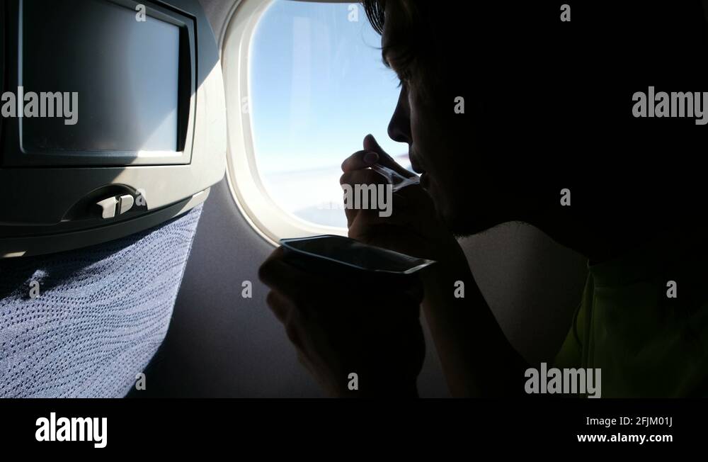 Man eats food with a fork while sitting by a window in an airplane in ...