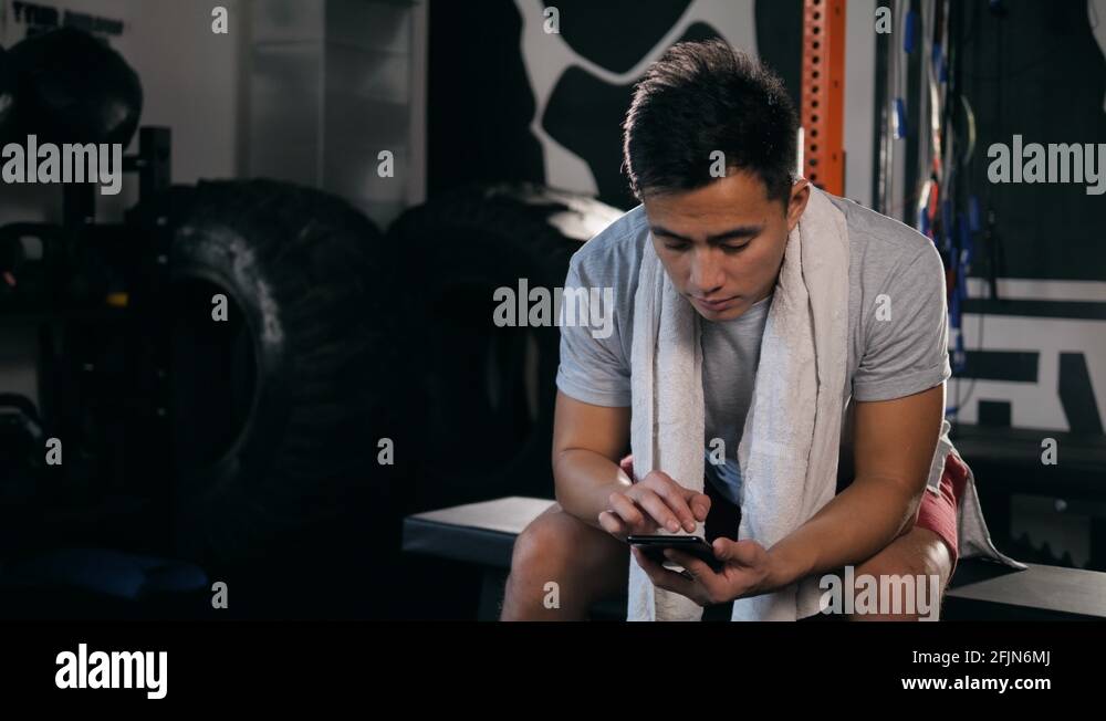 Tired asian korean young man using his mobile in the gym. Student boxer ...