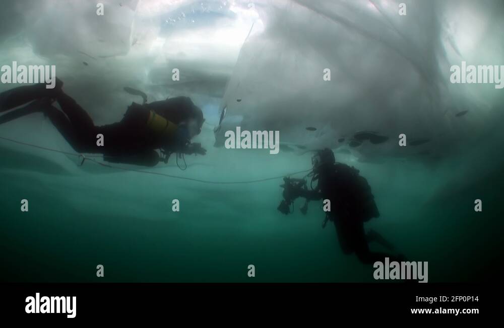 Diver with underwater cameraman under ice in cold water of lake Baikal ...