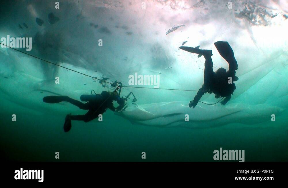 Underwater cameraman with camera and technical diver under ice of lake ...