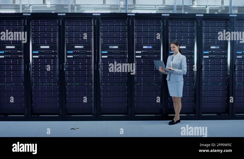 Female Data Center IT Engineer Works on Laptop Computer Next to Server ...