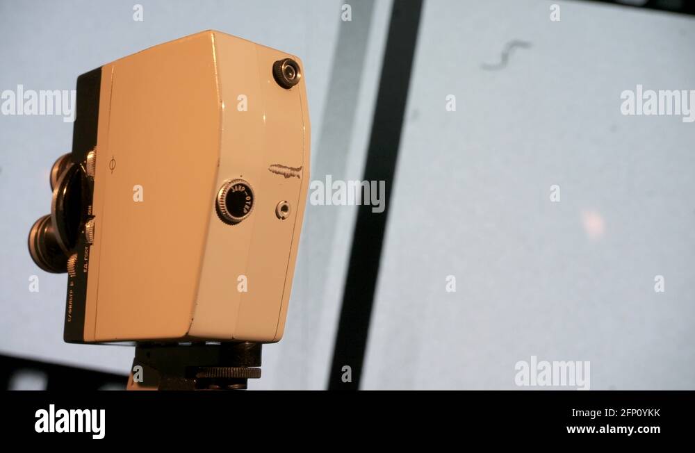 Vintage 8mm movie camera rotating in front of flickering film strip ...