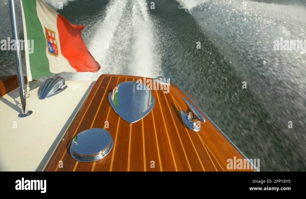 A classic luxury wooden runabout boat with an Italian flag on a lake ...