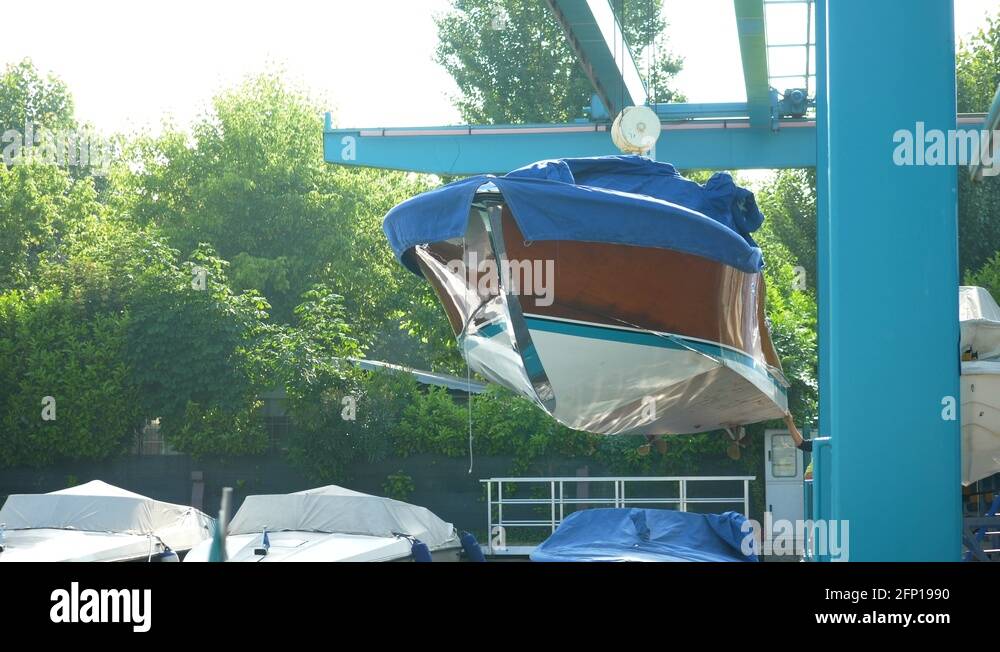 A classic luxury wooden runabout boat lowered with a crane in a marina ...