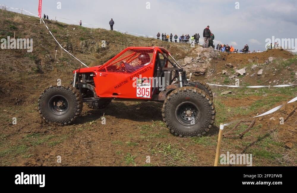 A red, modified 4x4 vehicle navigates a dirt hill and hole obstacle at ...