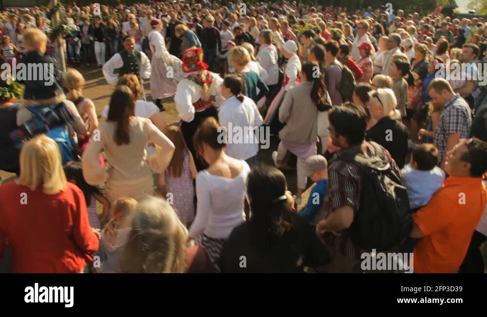 Hundreds of people dance joyfully around the big wooden Midsummer ...