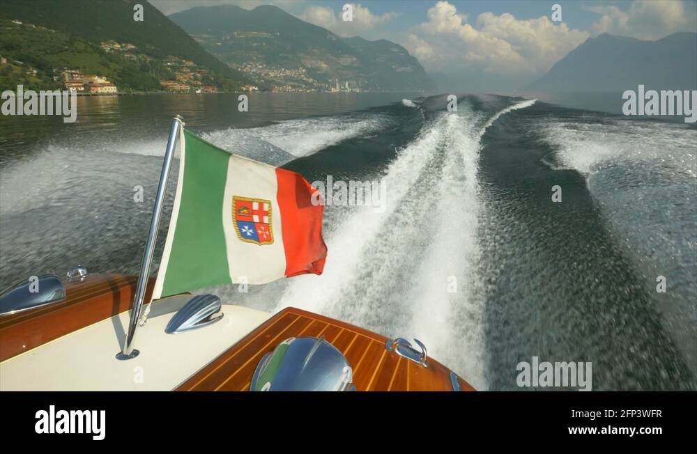 A classic luxury wooden runabout boat with an Italian flag on a lake ...