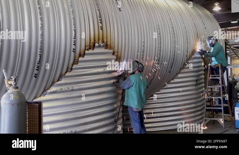 Two men welding large corrugated metal pipe with cameraement to the ...