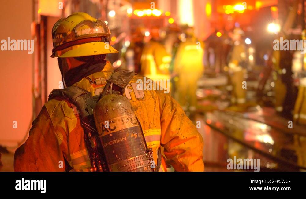 Fireman with oxygen tank fighting to put out a house fire at night in a ...