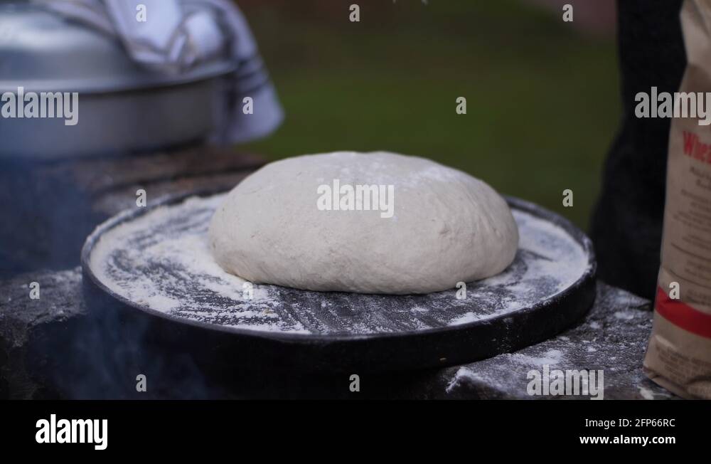 Pouring flour on raw braai bread dough next to open fire. Traditional ...