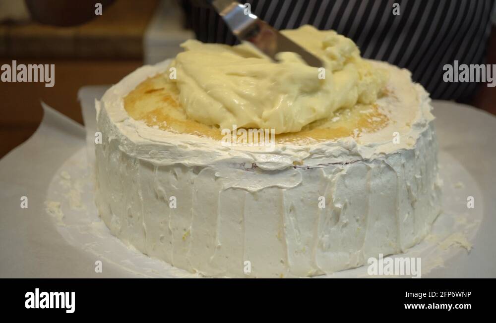Spreading yellow custard topping on top of rotating vanilla cake, Close ...