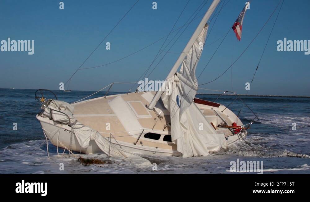 A shipwrecked sail boat washed ashore after a storm. Broken sails, worn ...