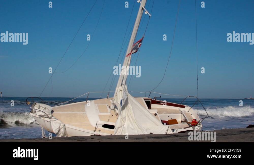 A shipwrecked sail boat washed ashore after a storm. Broken sails, worn ...