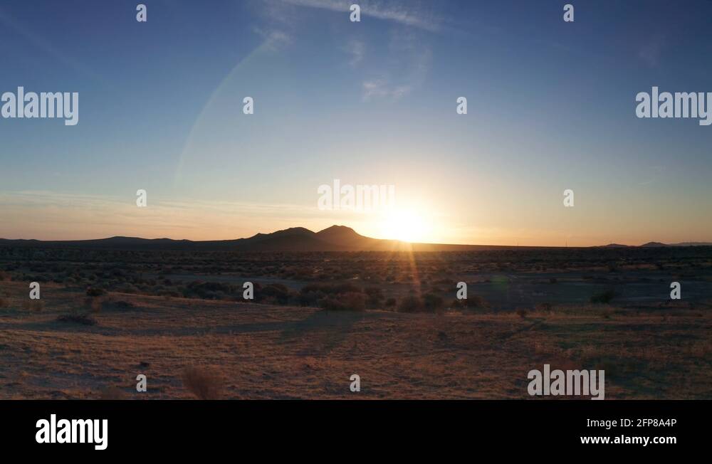 Bright sun on horizon casting light rays over golden Mojave Desert ...