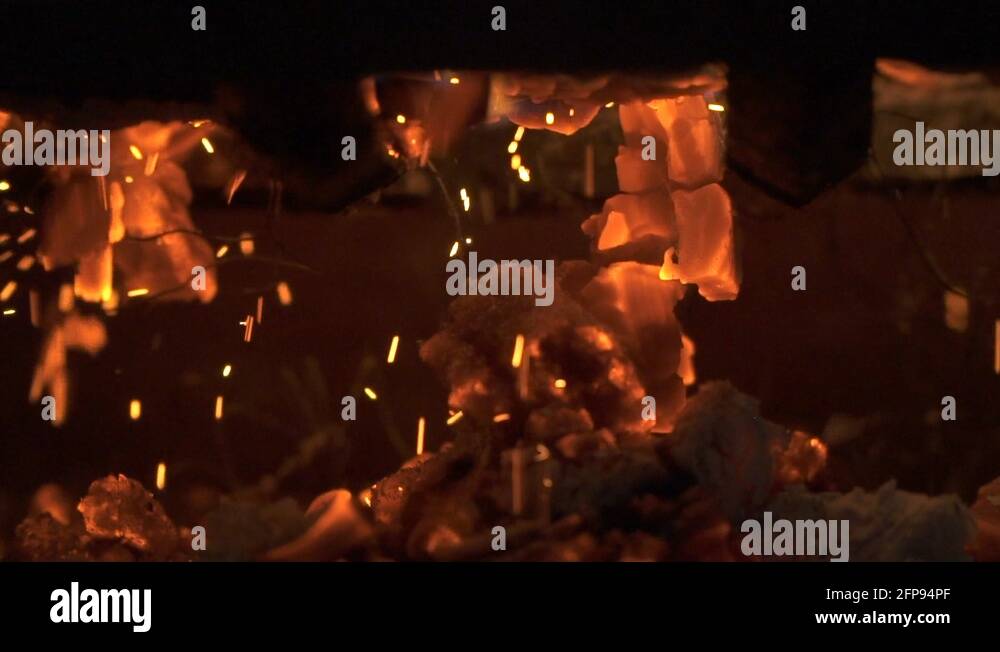 Burning embers and ashes falling through fireplace grate, slow motion ...