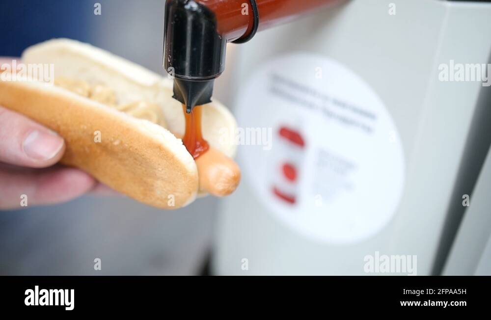 Ketchup pouring a hot dog with sausage from a vending machine in a fast ...