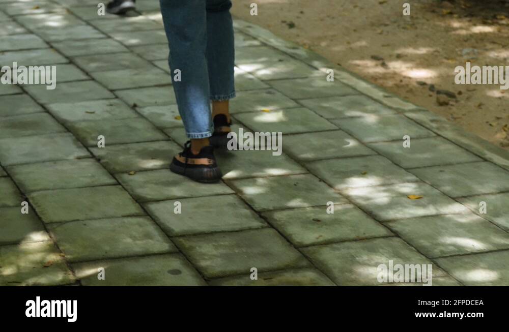 Close up of woman legs walking in shade on brick tiles at park in ...