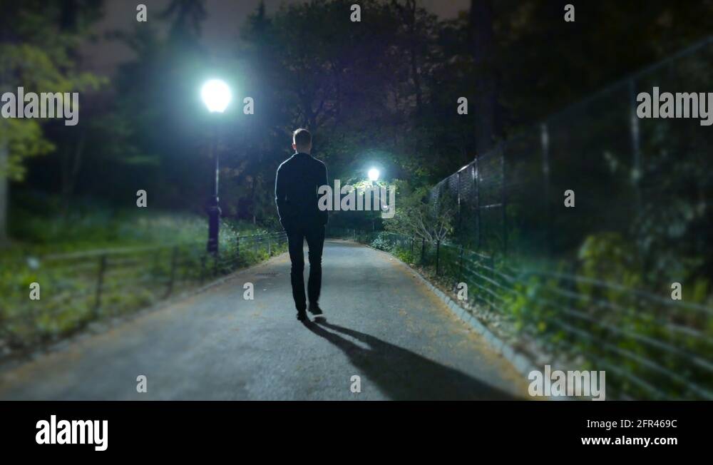 one man walking alone trough city park at night. spooky scary ...