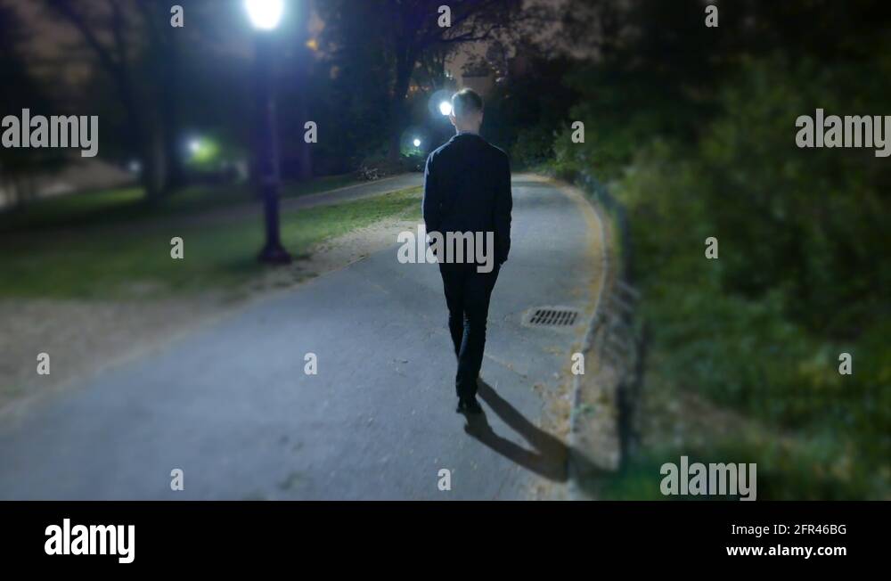one man walking alone trough city park at night. spooky scary ...