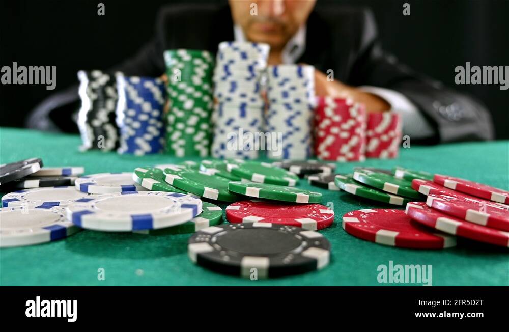 A gambler at a poker table peeks at his cards and bets a stack of chips ...