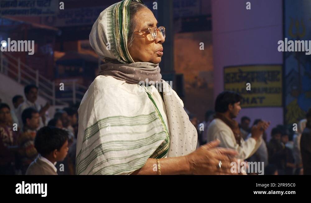 Elderly Indian woman clapping durring an incense offering to the Ganges ...
