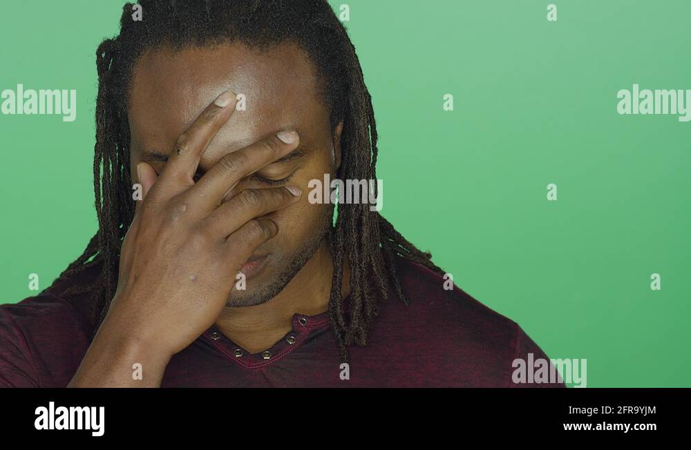 A black man with dreads looking sad and covering his face with his ...