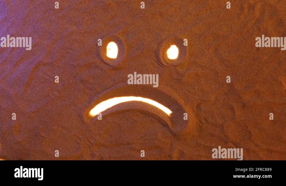 Hand drawing Sad Smile symbol in the sand. Beach background. Top view ...