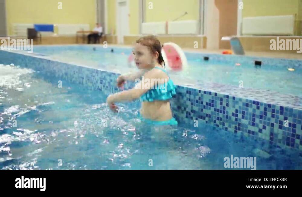 Happy little girl in swimsuit dances in pool and boy swims near she ...