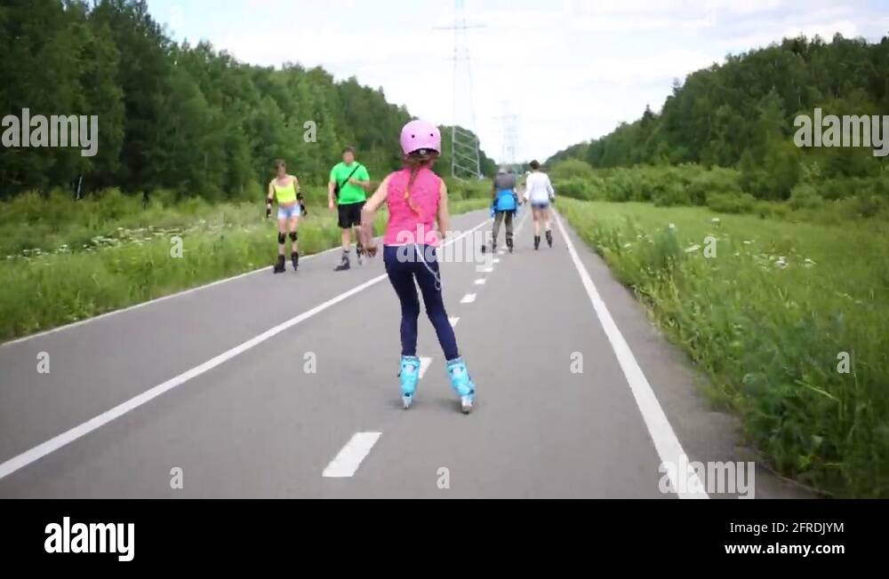 Girl blue helmet and pink roller riding snake on bike path in park ...