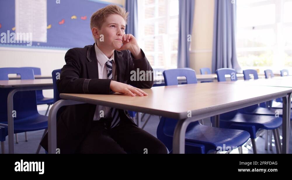 4K Unhappy little boy sitting alone in school classroom with worries on ...