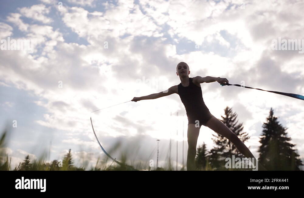 Dance young gymnast with ribbon on sunset sky background. Rhythmic ...
