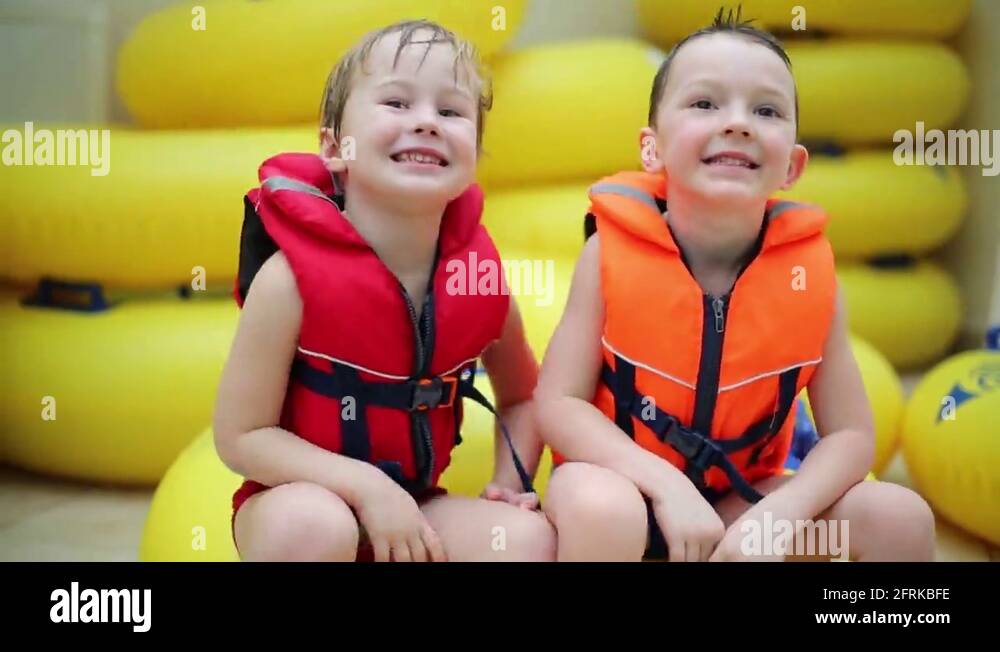 Two boys in life jackets jump on a big inflatable ring in the aquapark ...